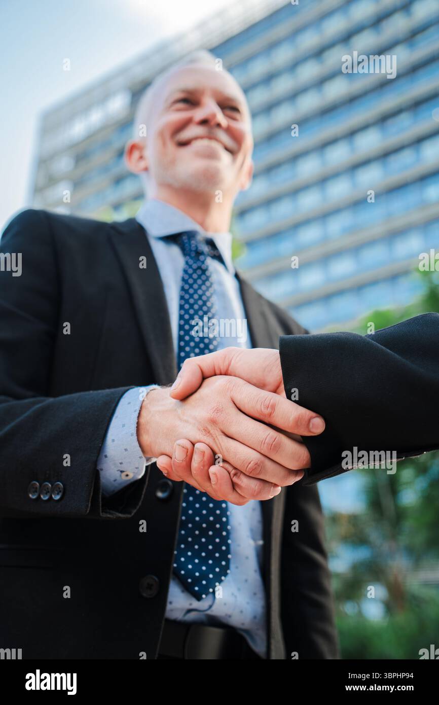 Two businessmen dressed in suits are engaged in a formal handshake ...