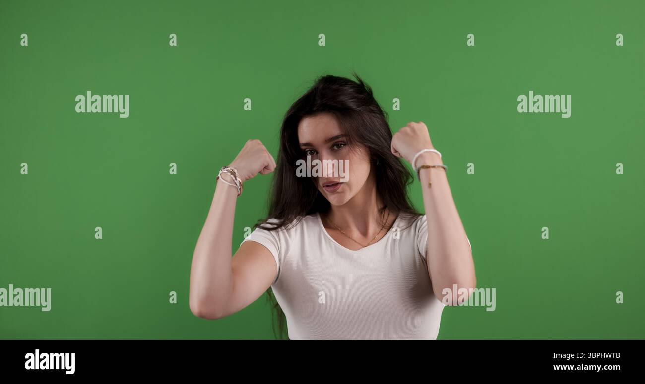 Strong young woman flexing her biceps on green screen background ...