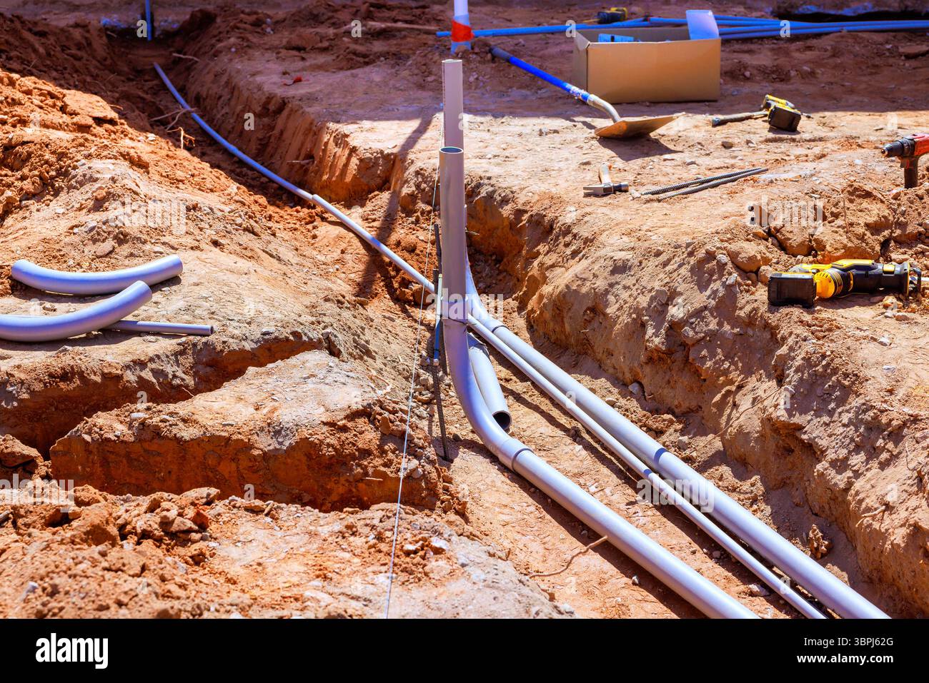 Workers install plumbing pipes in trench at construction site under ...