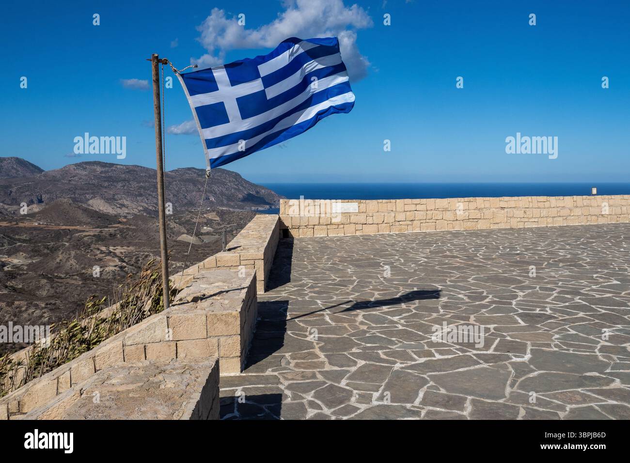 Greek flag waving in the wind on a viewpoint overlooking mountains and ...