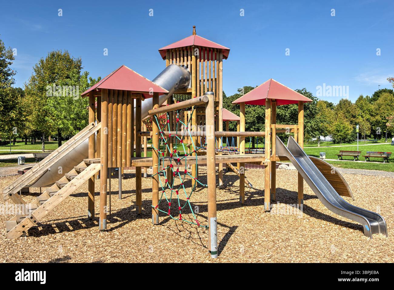 A deserted, wooden climbing castle with slide, balancing poles, towers ...