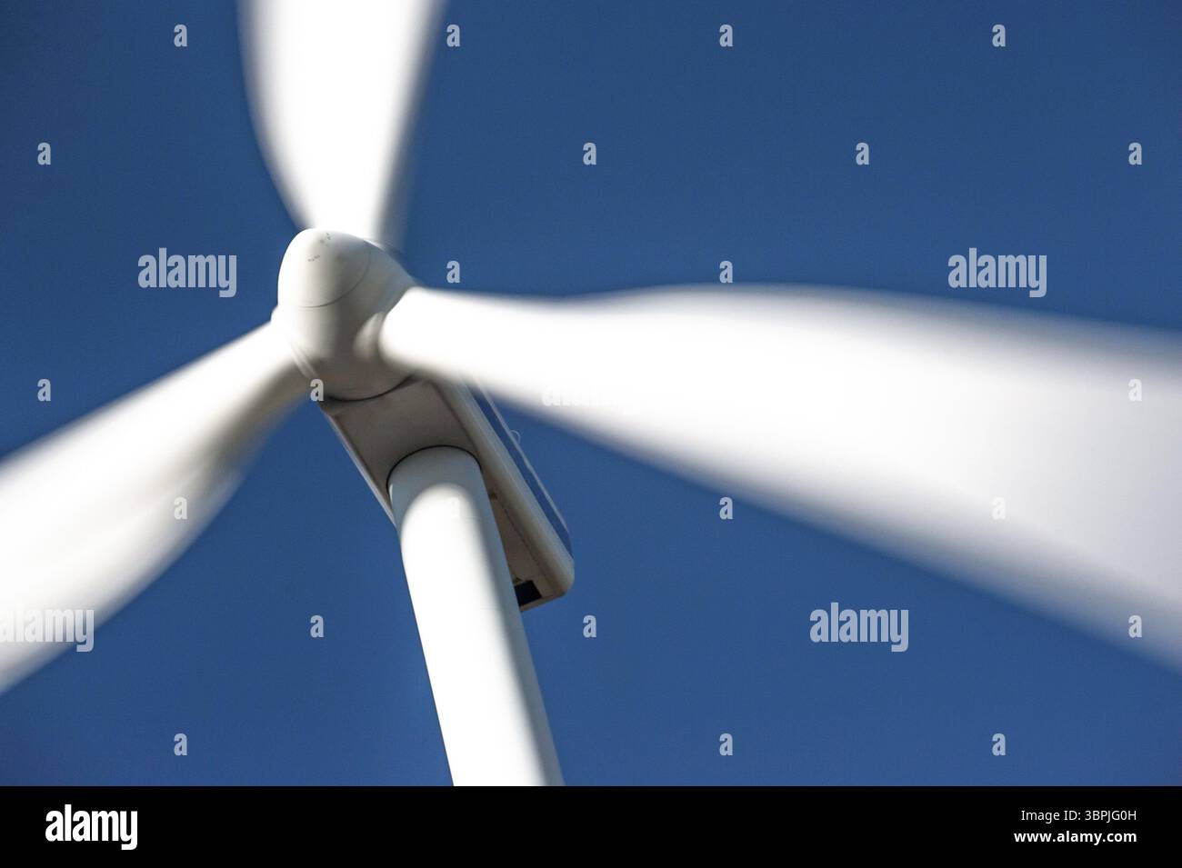 White rotor blades of a wind turbine blurred by motion blur against a ...