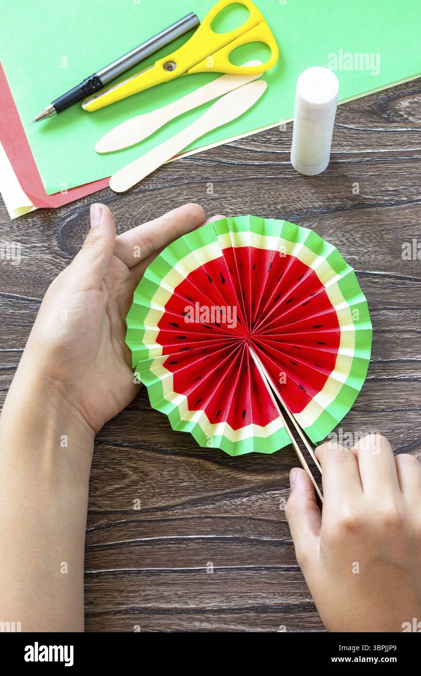In the hands of a child Paper Fan watermelon on a wooden table ...