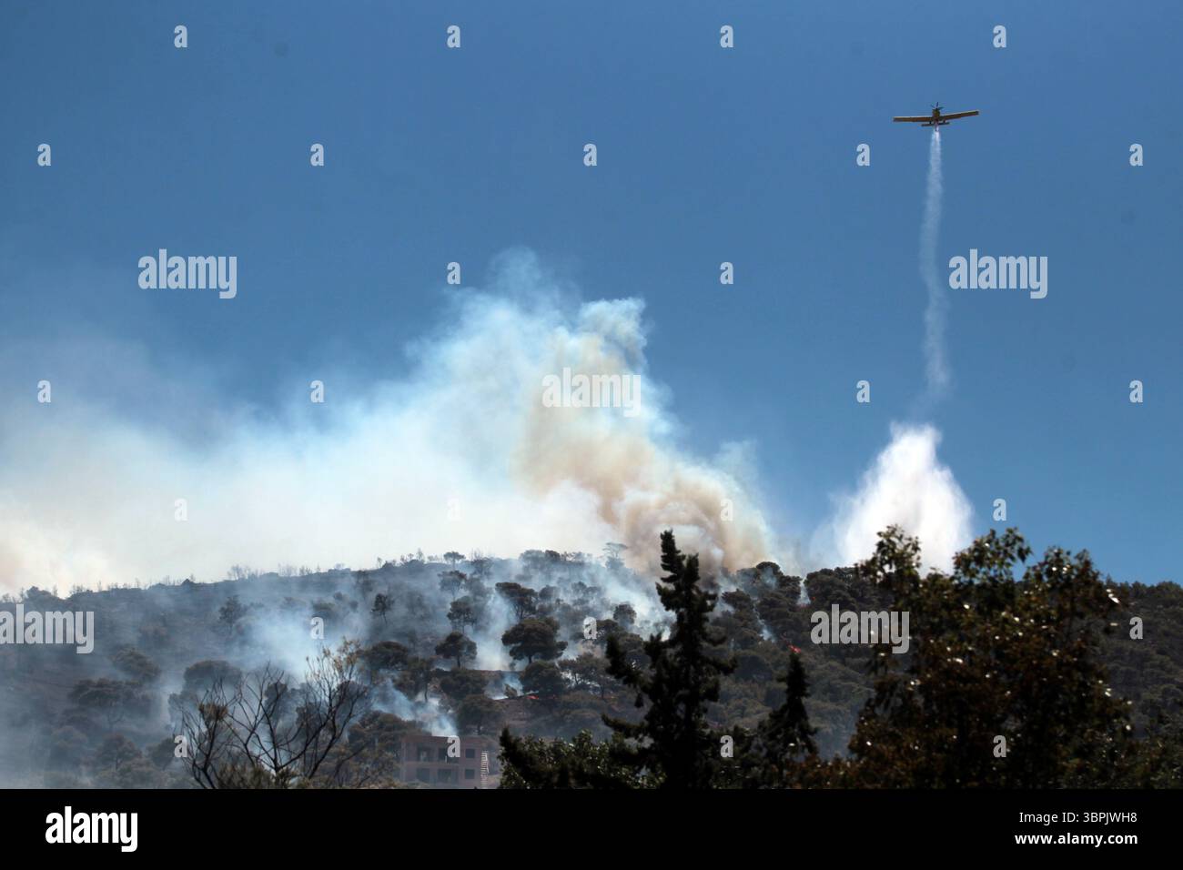 A firefighting airplane drops water as a wildfire burns at Aghios ...