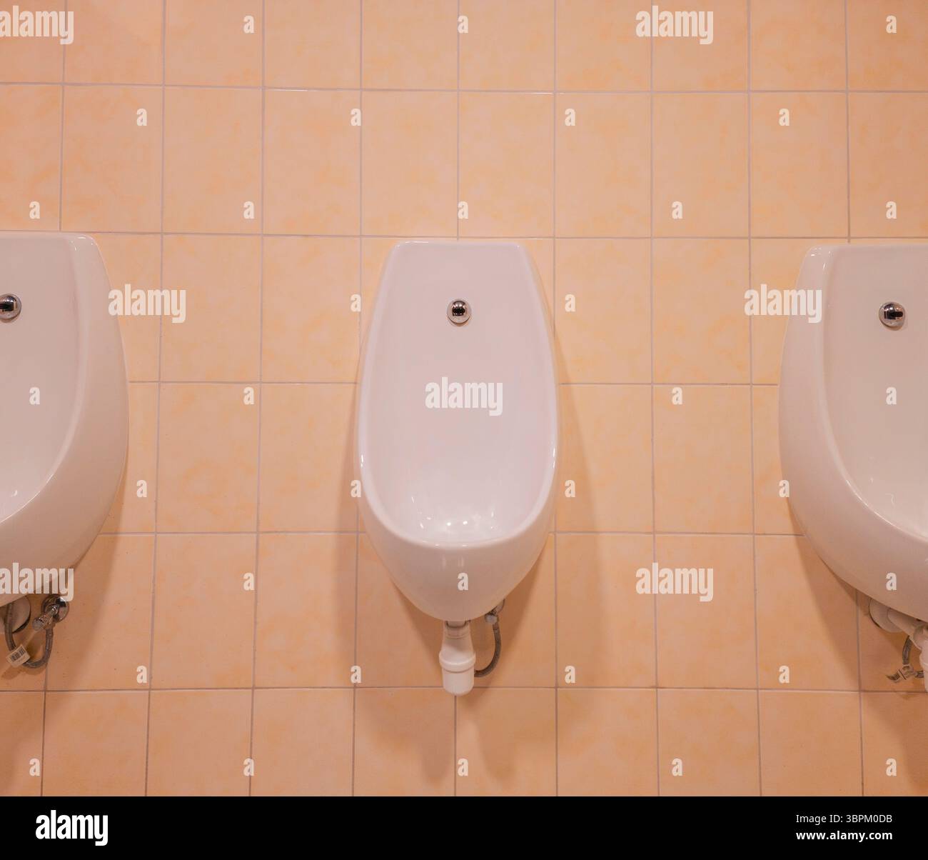 Three white urinals are positioned against a cream-colored tiled wall ...
