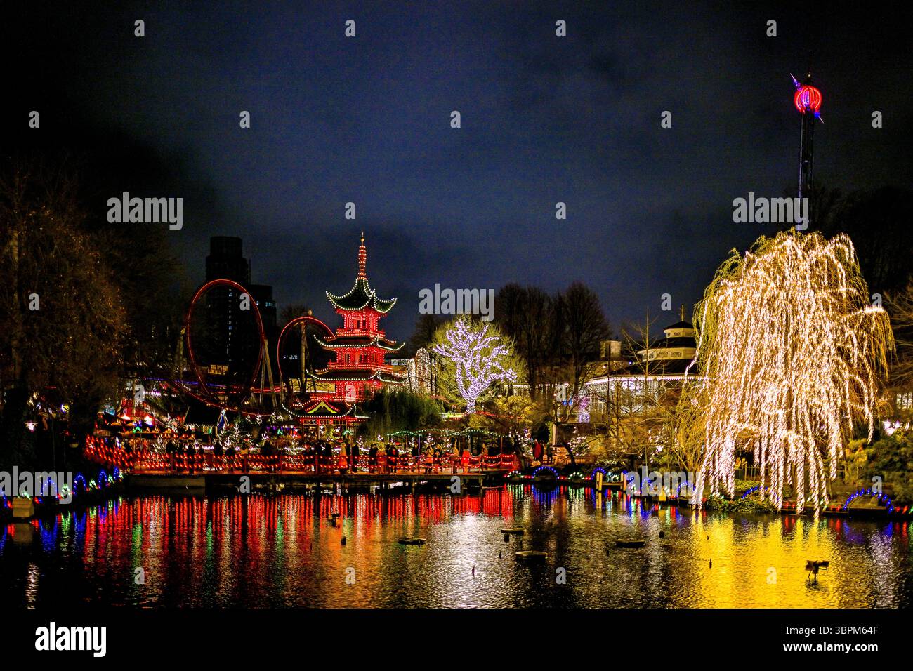 Wide view of Tivoli Gardens at night with illuminated pagoda, lake, and ...