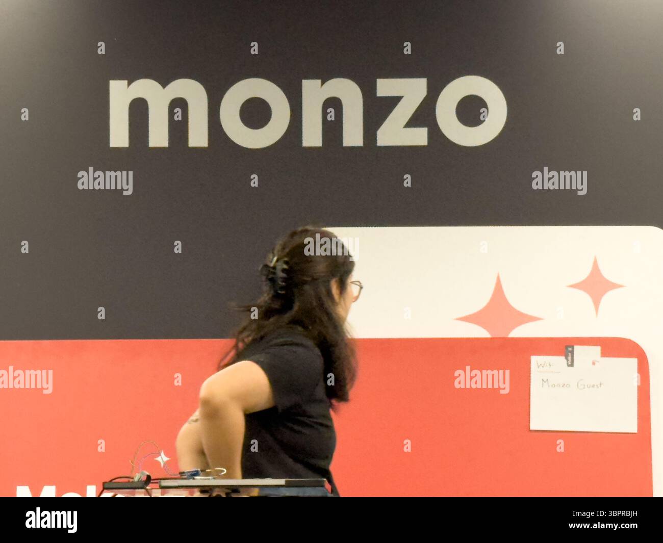 Woman Presenter Prepares for Tech Talk on Stage with Monzo Logo ...