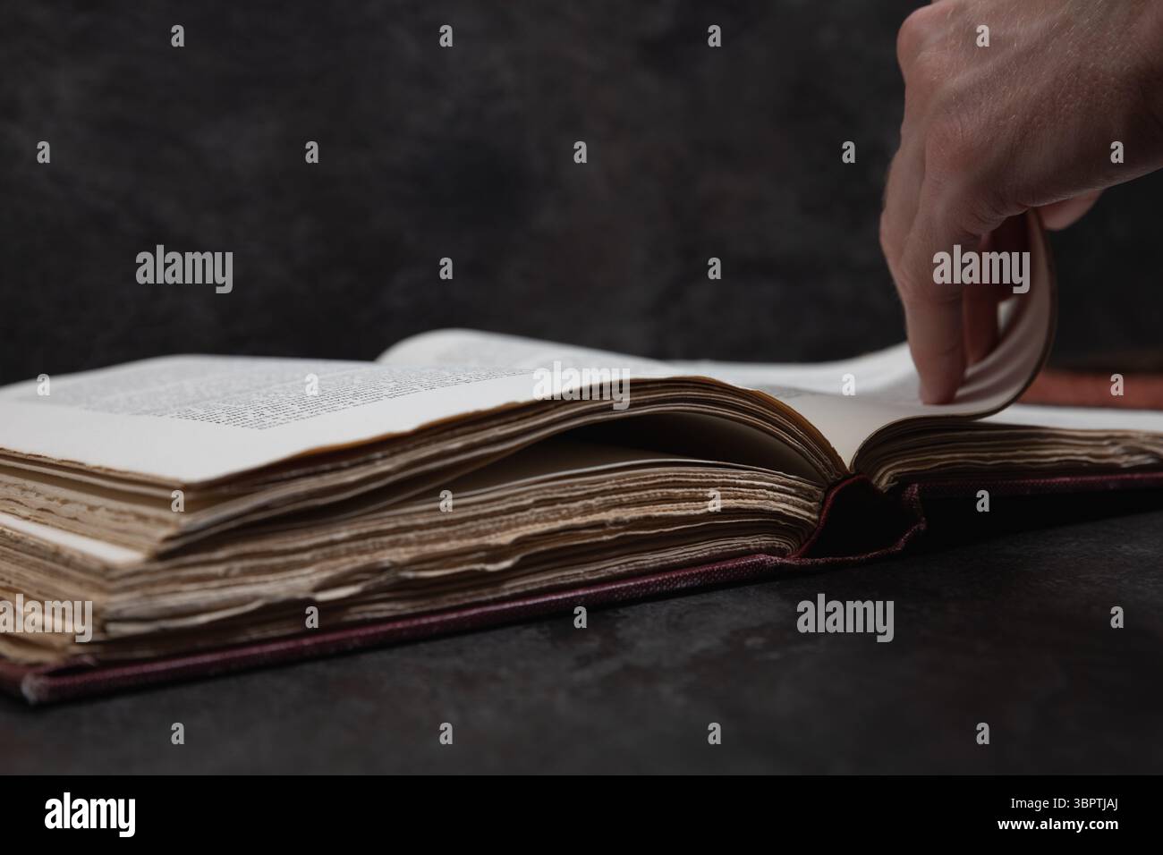 Open antique book lying on dark surface with dark background, a hand ...