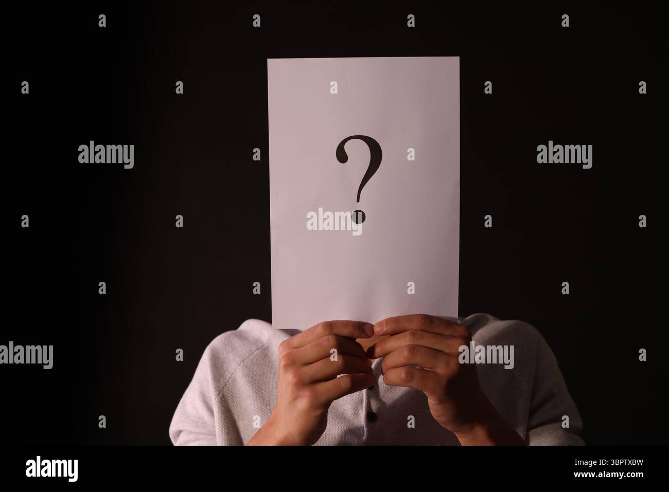 Man hiding behind paper sheet with question mark on dark background ...