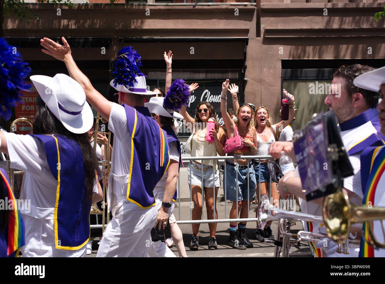 A marching band in white and purple uniforms with rainbow accents ...