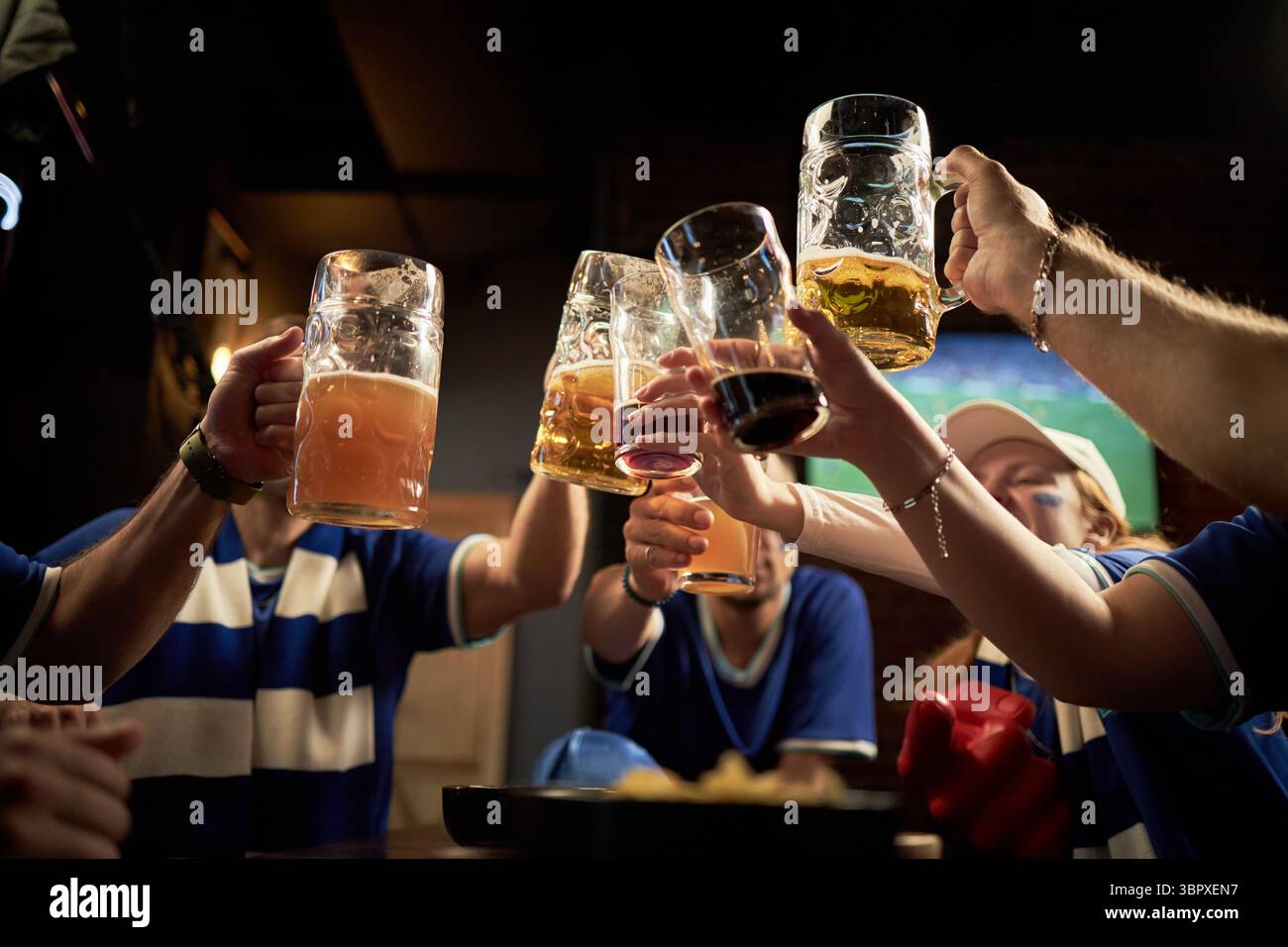 Group of young soccer fans raising beer mugs and toasting in pub in ...