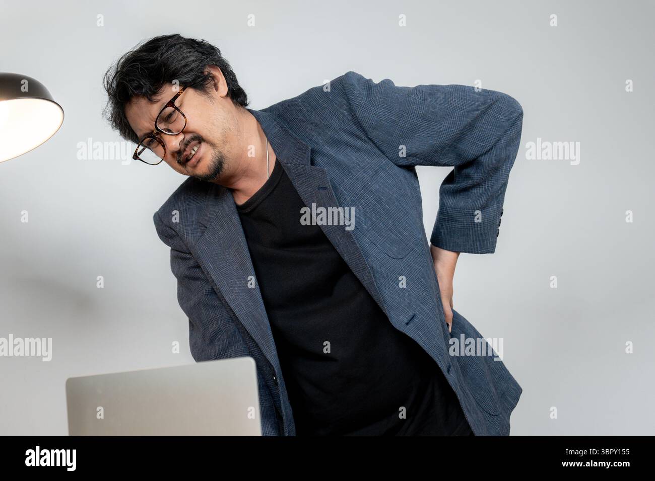 Asian male office employee with back pain from prolonged sitting ...
