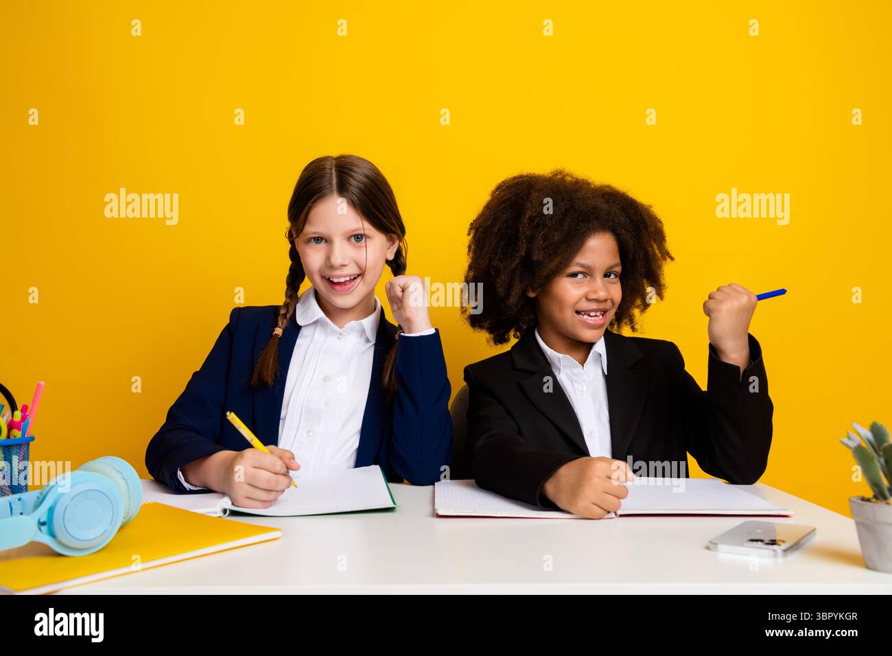 Two happy schoolgirls studying together in classroom wearing uniforms ...