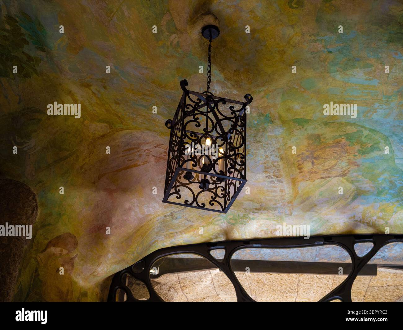 An ornate wrought-iron lamp hangs from a ceiling with floral murals in ...