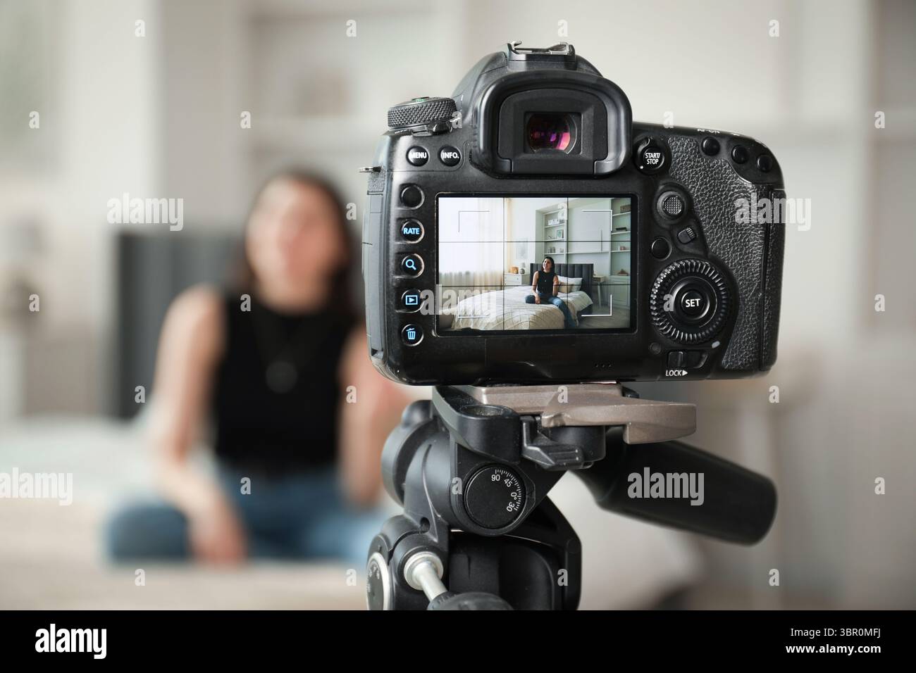 Woman sitting on bed in studio, focus on video camera recording her ...