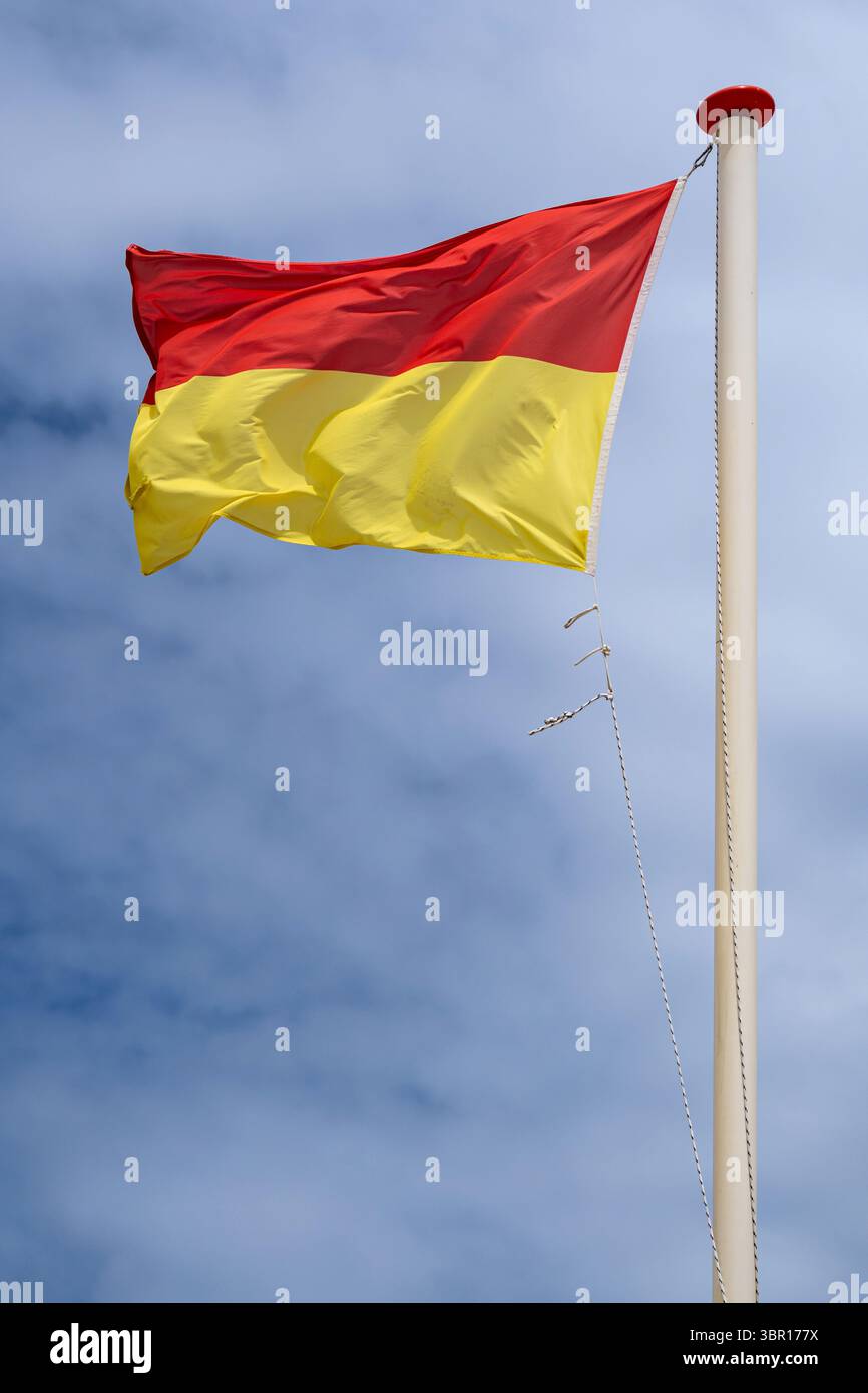red and yellow lifeguard on duty flag on the beach in the Netherlands ...