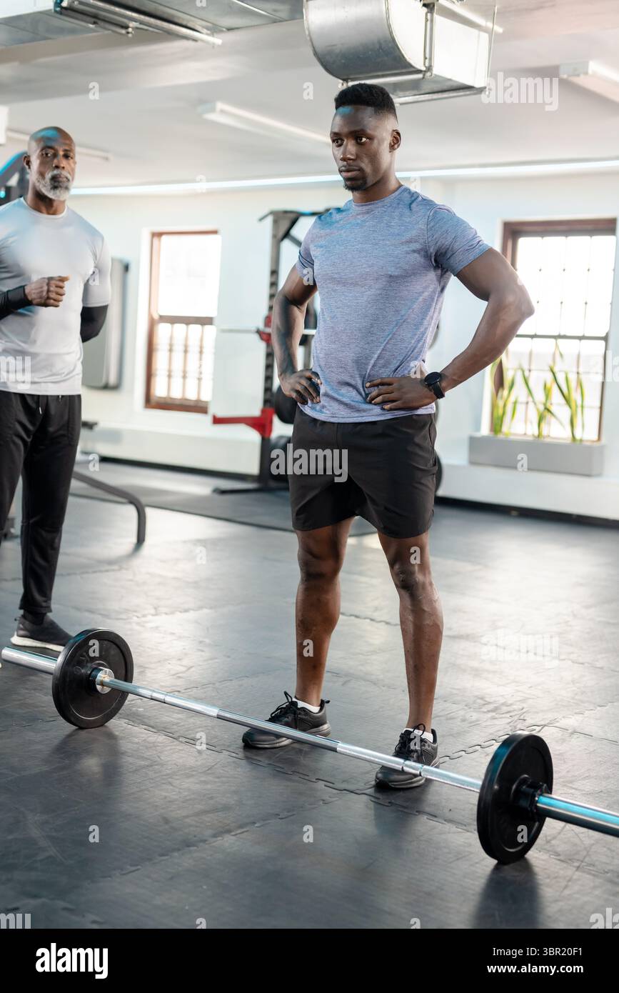 African American trainer and client performing squat workout at fitness ...