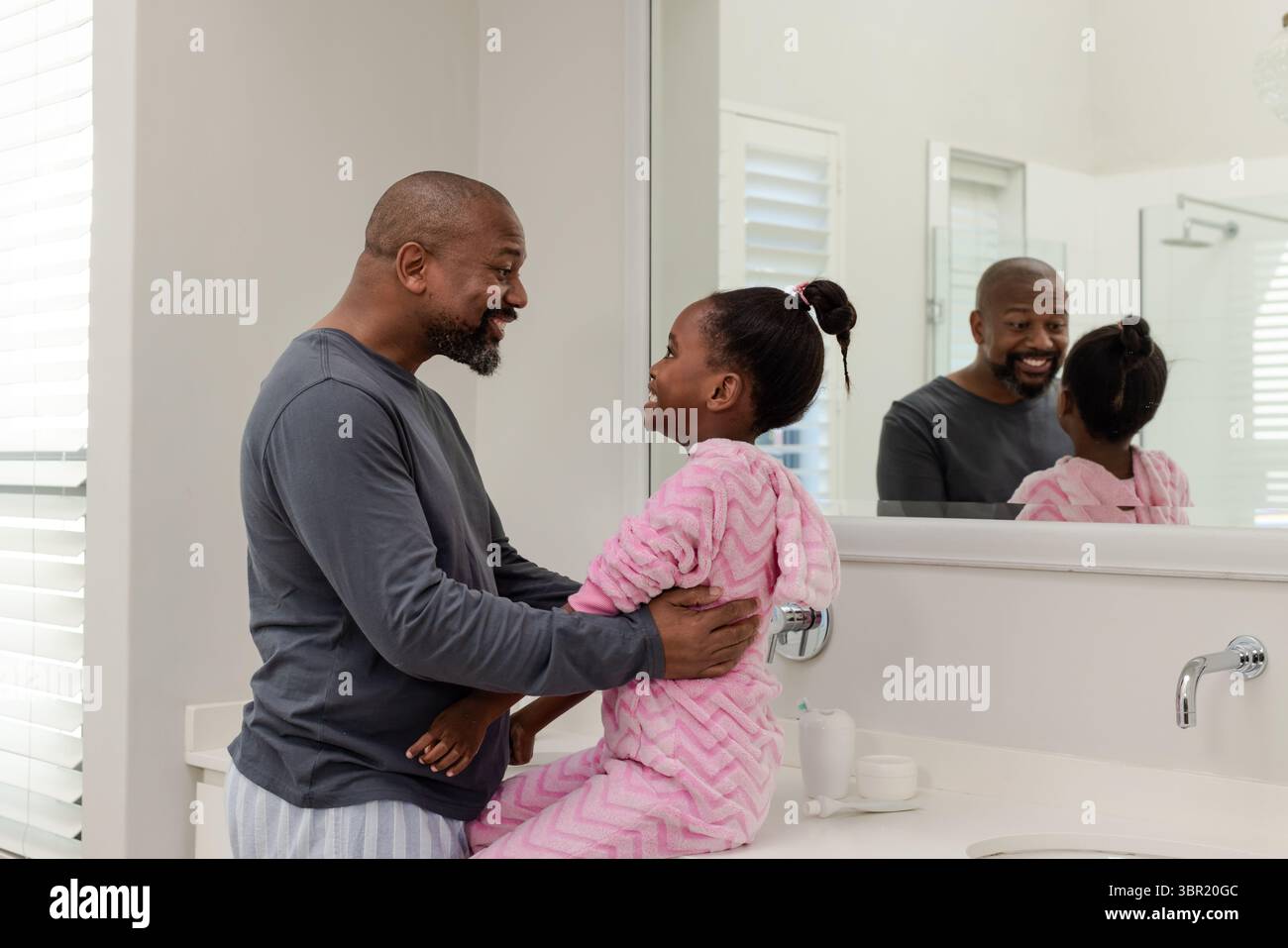 African American father holding daughter in pajamas on bathroom vanity ...