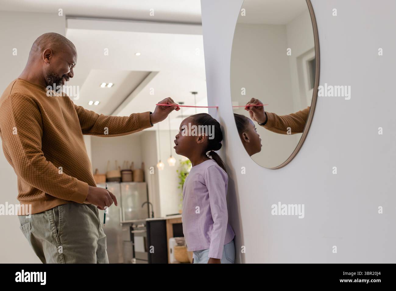 African American father and daughter measuring height in hallway by ...