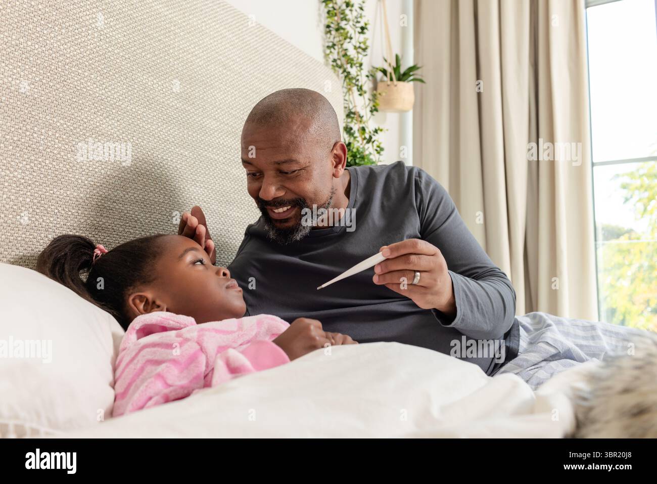 African American father and daughter lying in bed checking temperature ...