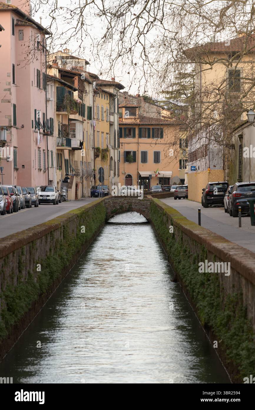 Canal in Lucca, Italy with stone pedestrian bridge and colorful ...