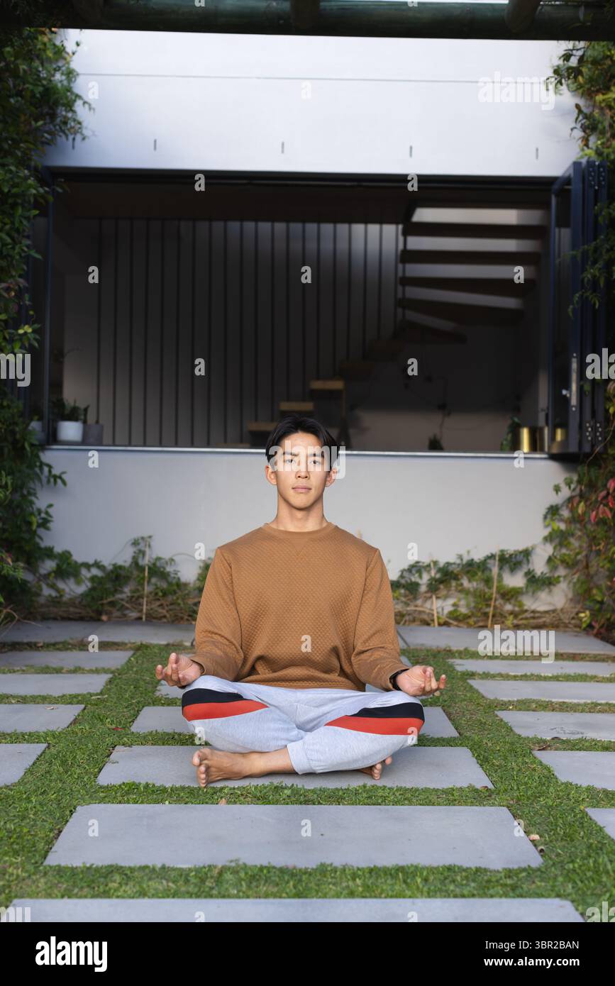 Asian man meditating cross-legged on stepping stones in lawn by sliding ...