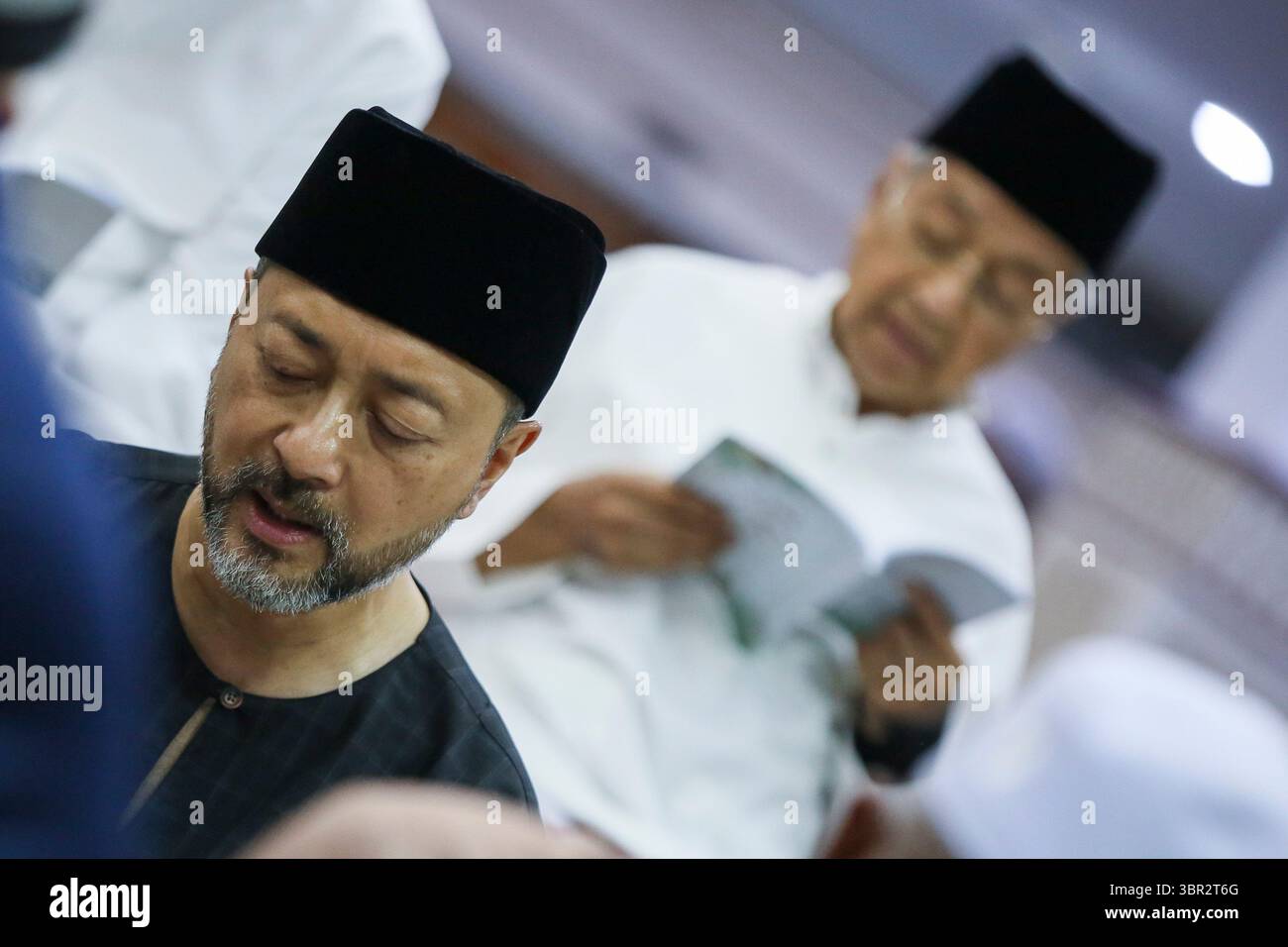 Mukhriz Mahathir reads a prayer booklet in front of Tun Mahathir at ...