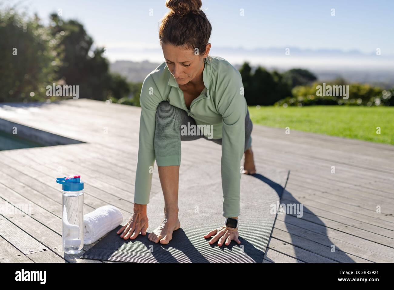 Woman performing forward lunge stretch on pool deck with yoga mat ...