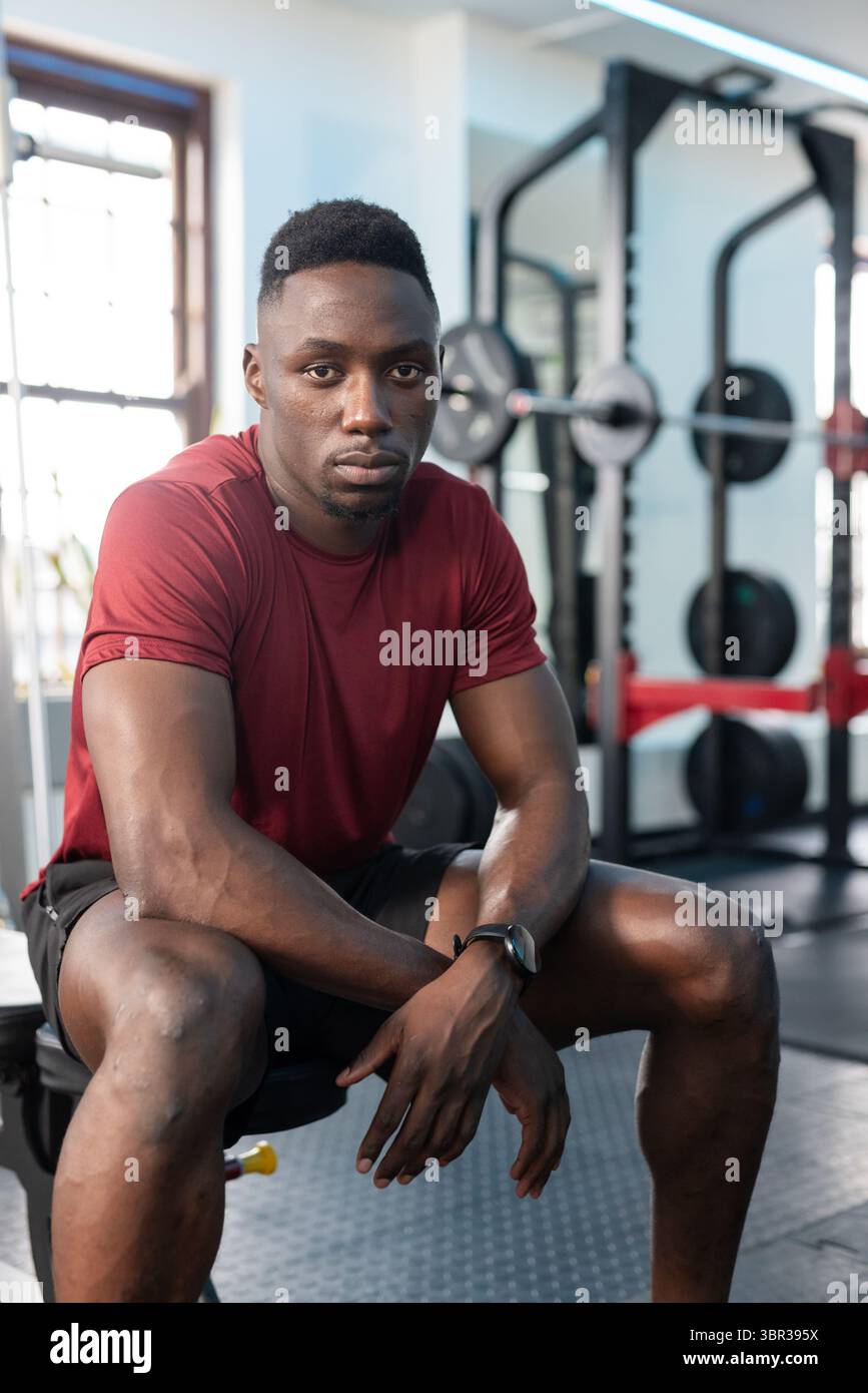 African American man sitting on weight bench in gym, resting arms on ...