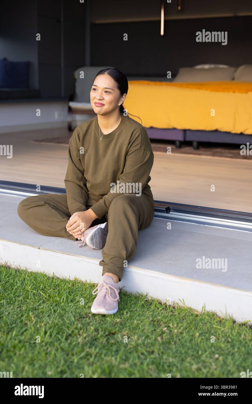 Asian woman sitting cross-legged on patio threshold by yellow bedspread ...