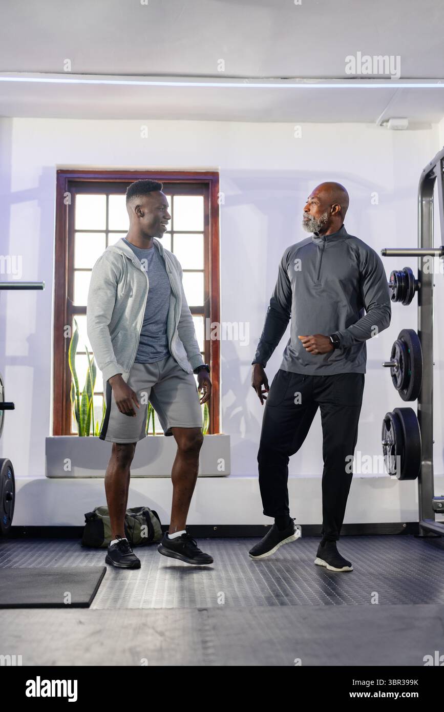 African American male trainer and client standing beside weight rack ...