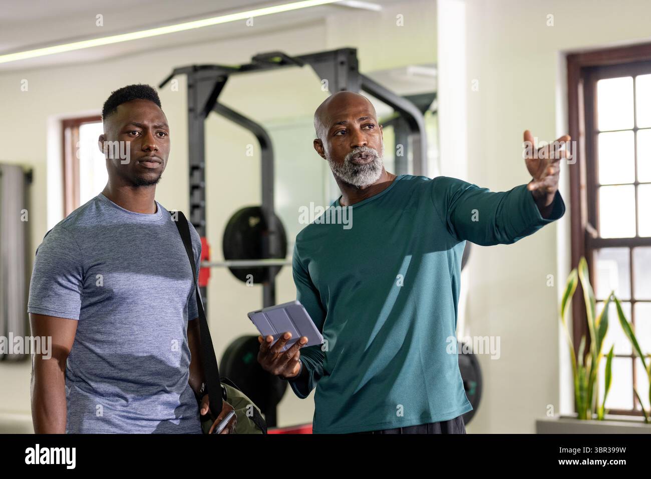 African American male trainer and client planning workout at gym with ...