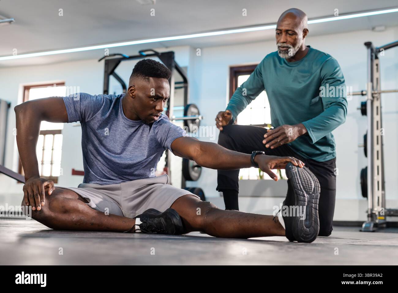 African American trainer guiding trainee stretching on mat in gym with ...
