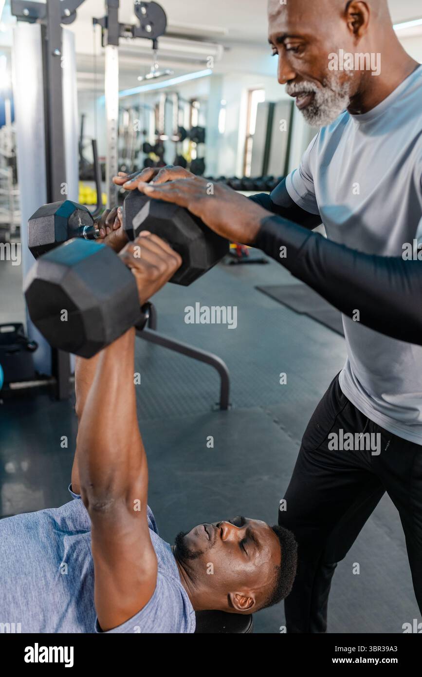 African American male trainer spotting client pressing hexagonal ...