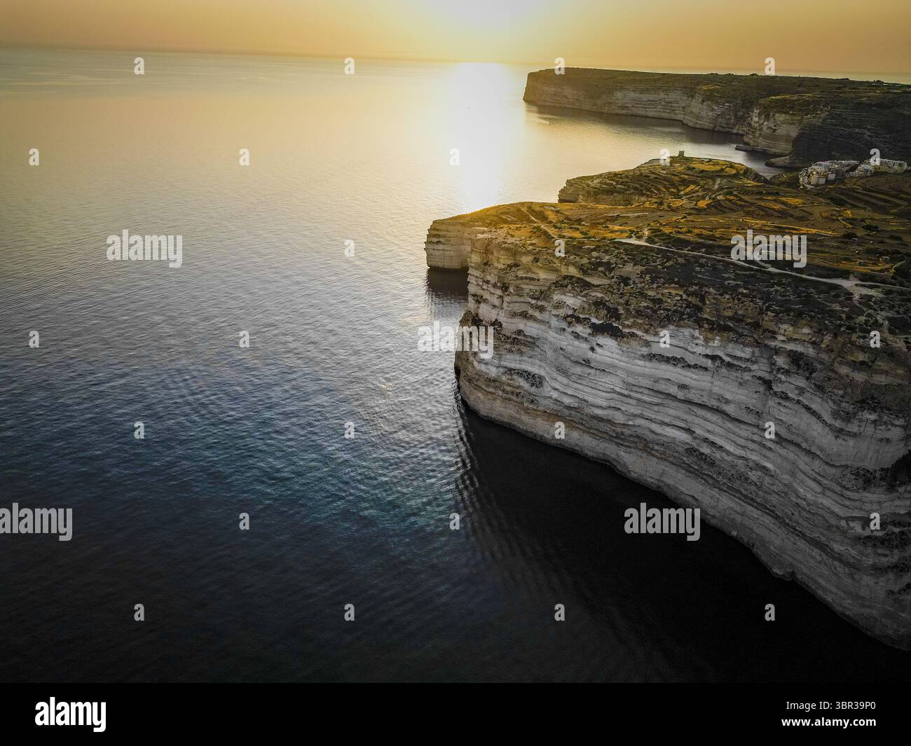 Aerial view of rugged cliffs meet the turquoise sea under a golden ...