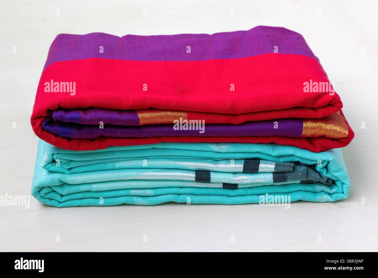 Two vibrant cotton sarees elegantly folded on a light wooden surface ...