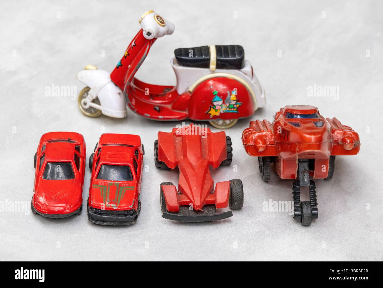 Collection of vintage red toys, including a scooter, metal sedan cars ...