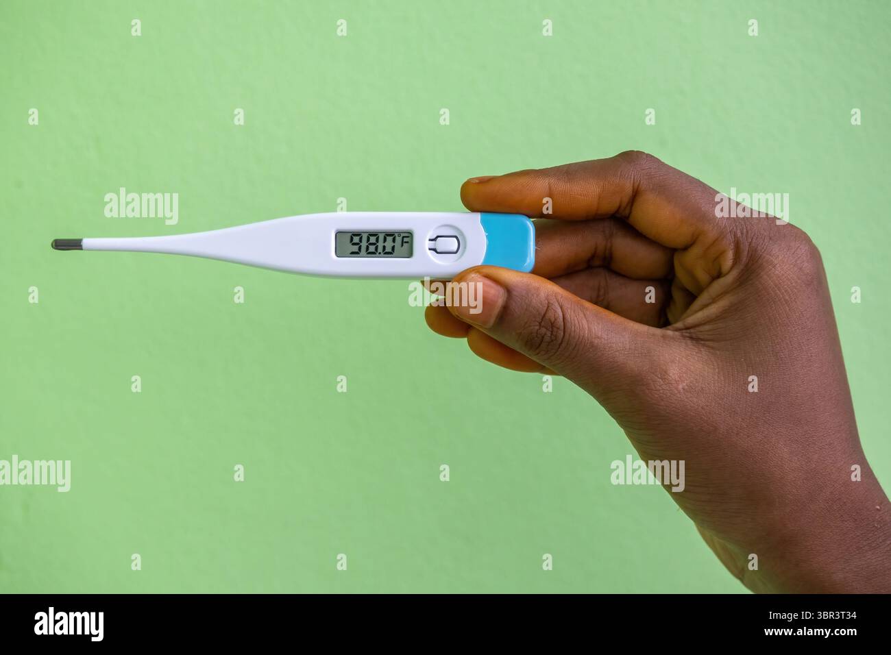 Female hand holding a digital thermometer on a green background. Normal ...