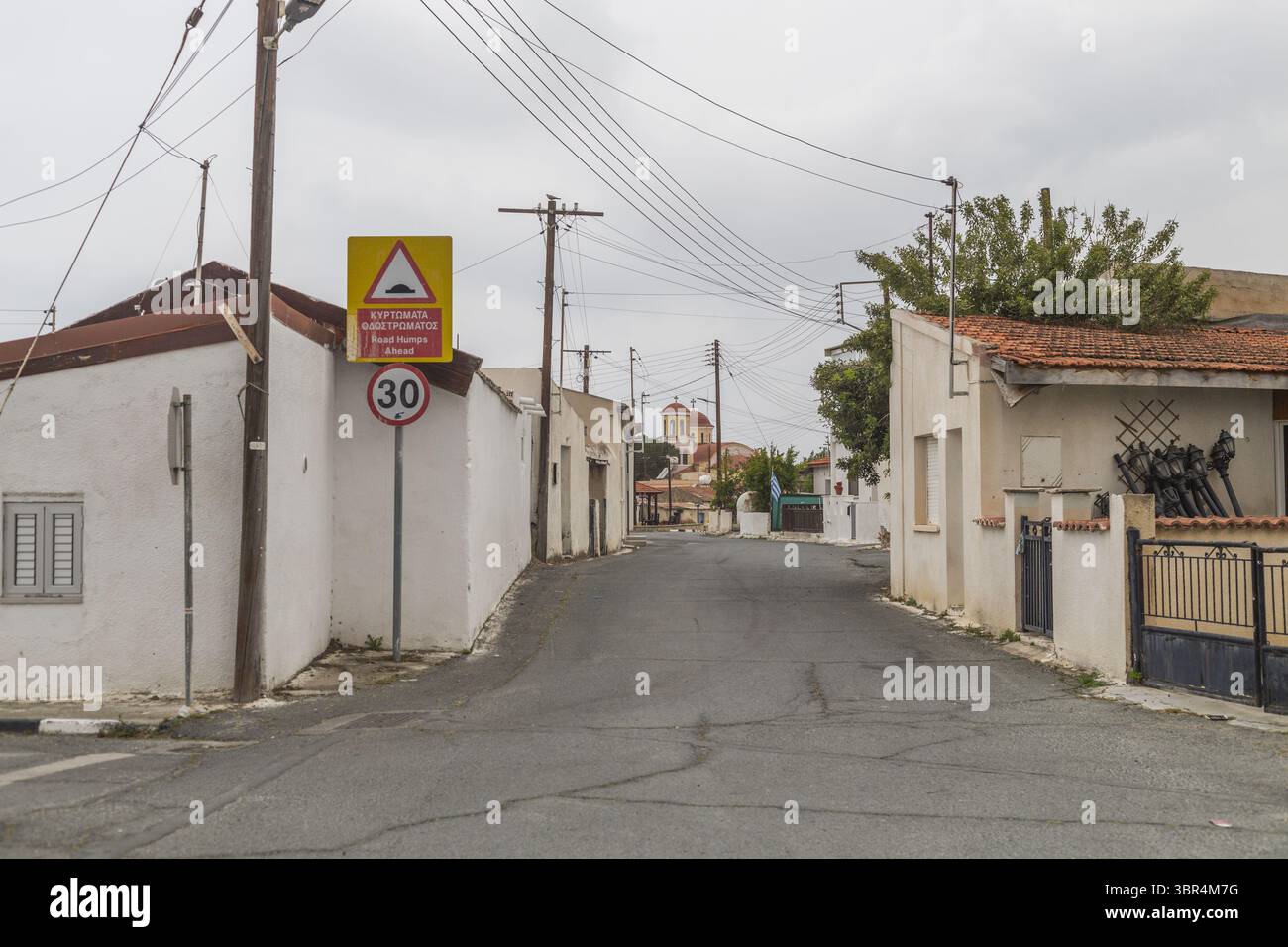 View of a quiet street winding past white buildings under a cloudy sky ...