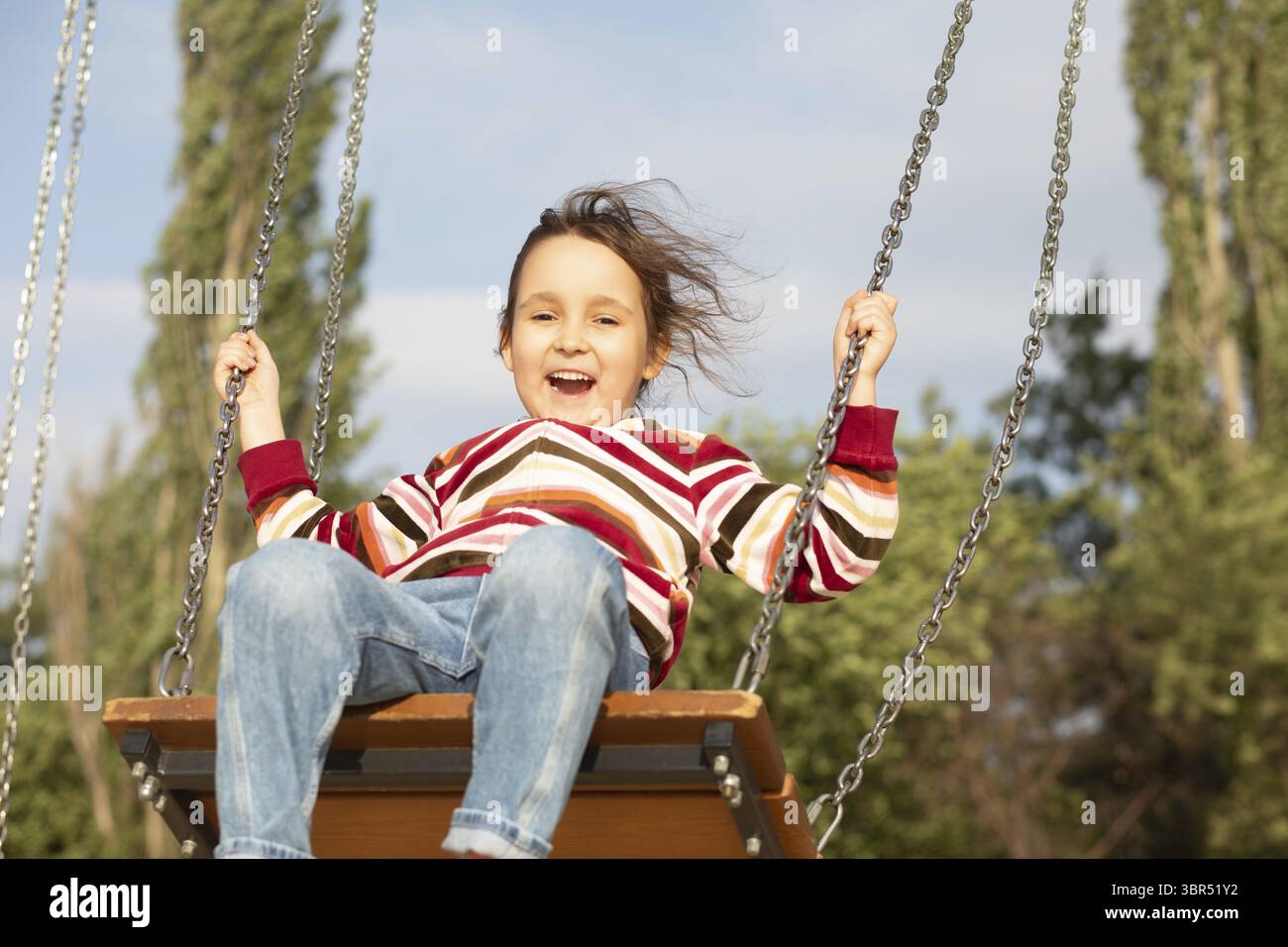 Smiling kid girl playing on a swing outdoor. Children summer activity ...