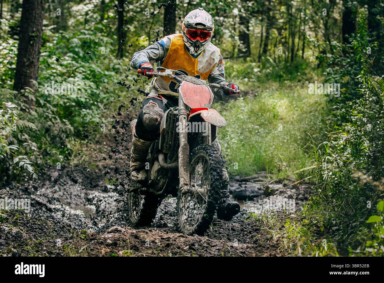 Enduro rider on dirt bike speeding through muddy forest trail during an ...