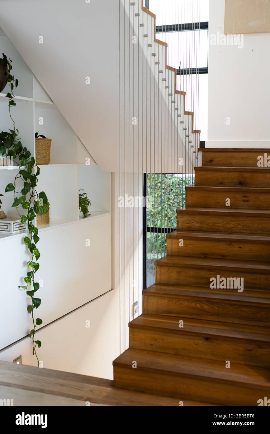 Wooden staircase rising inside stairwell, with cable railing beside ...