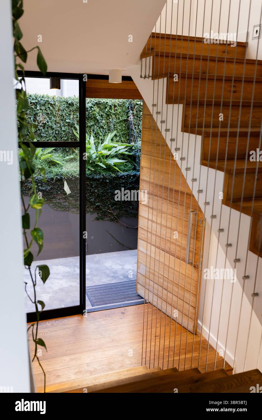 Wooden staircase with steel cable railing rising upward, facing black-framed door and green ...
