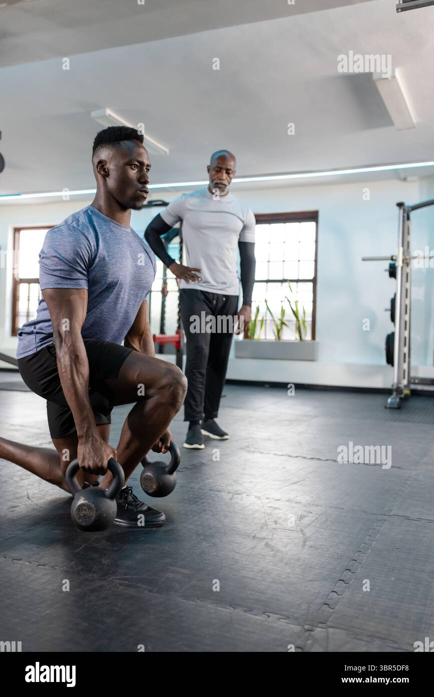 Senior African American trainer guiding client performing weighted ...