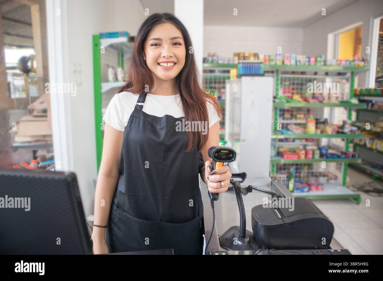 Smiling young Asian woman as grocery store staff standing at cashier ...