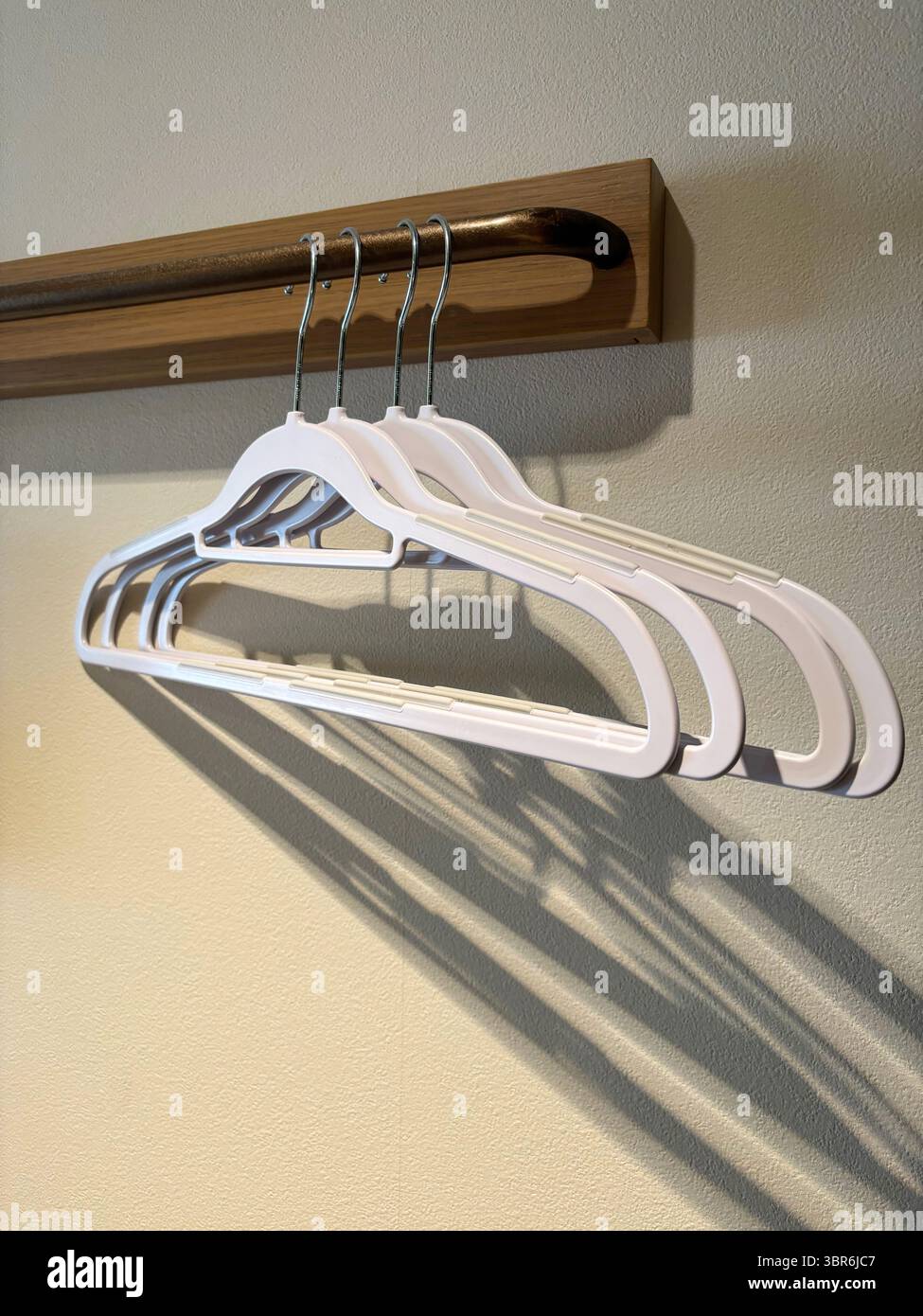 4 modern and sleek cloth hangers, hanging on a single rod attached to ...