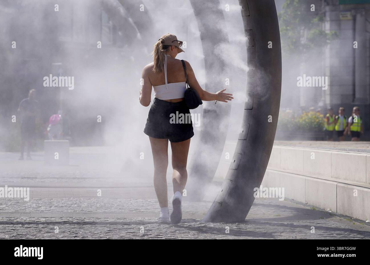 A lady cools off as she walks through a cooling water feature spraying ...