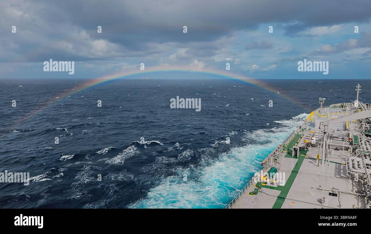 Large cargo ship sailing under double rainbow in the ocean. Tanker ...