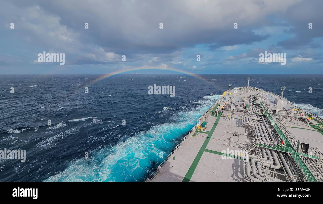 Large cargo ship sailing under double rainbow in the ocean. Tanker ...