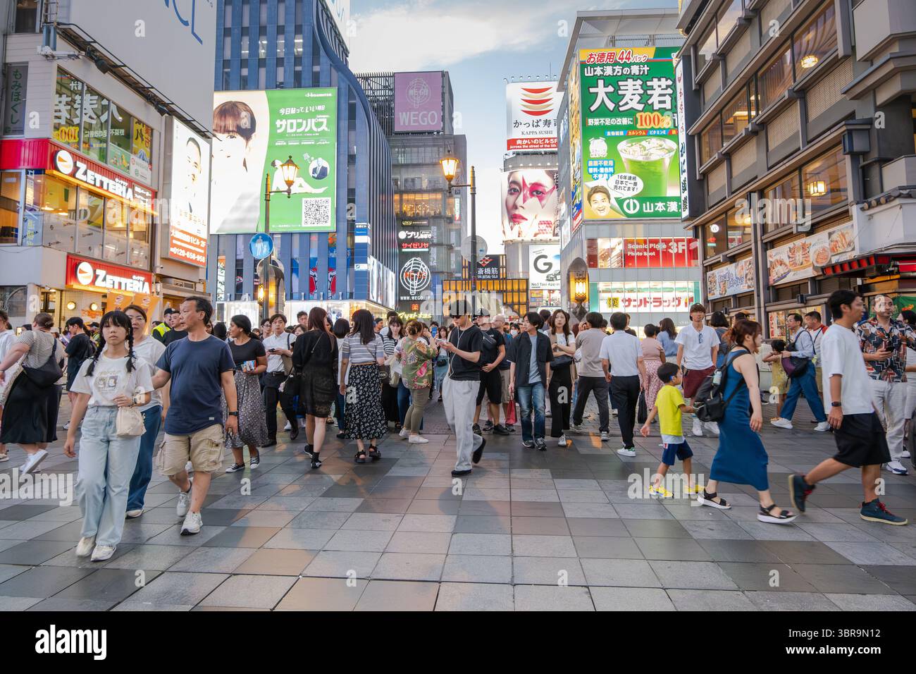 A densely packed crowd walks through the illuminated Dotonbori district ...
